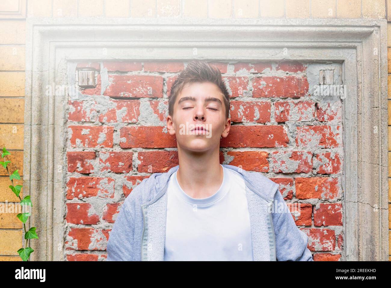 Portrait of a teenage boy leaning against a wall, with closed eye's ...