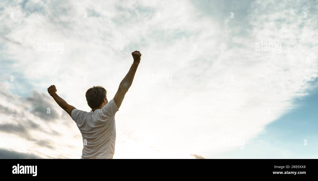 Young man standing with his arms raised high in triumph under white ...