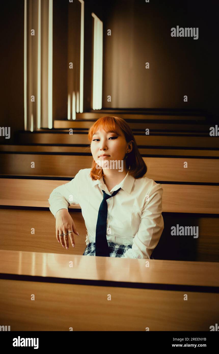 A ginger Asian student in uniform, sitting at a desk in an empty ...