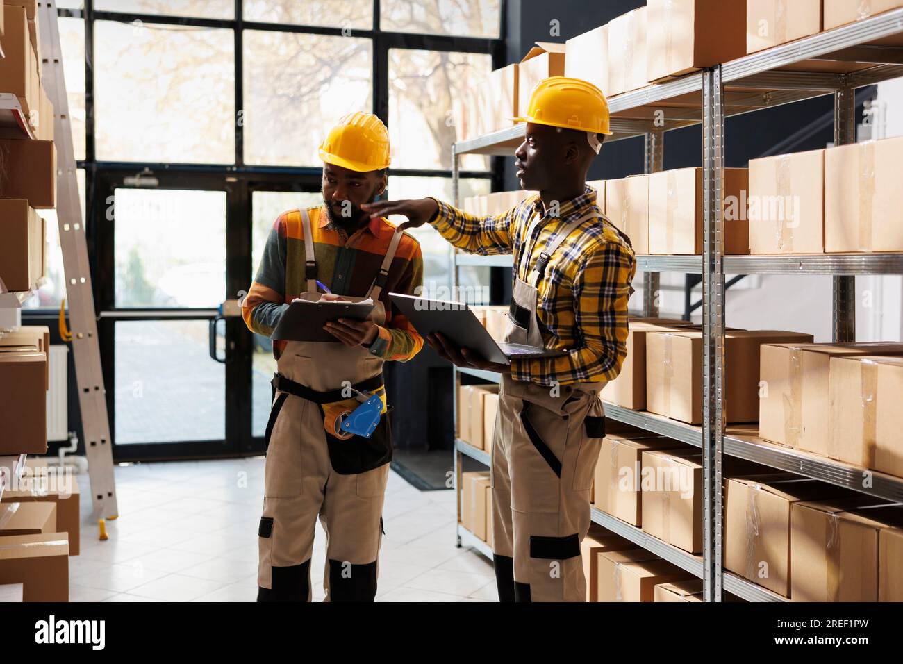 Warehouse coworkers using laptop inventory software and writing in ...