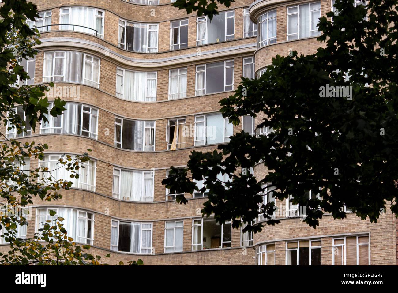 A large brick building behind trees Stock Photo - Alamy