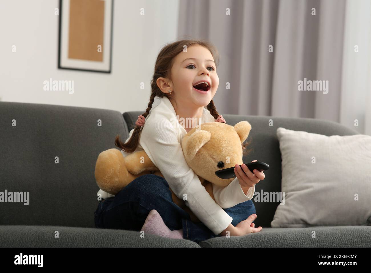 Happy girl changing TV channels with remote control on sofa at home ...