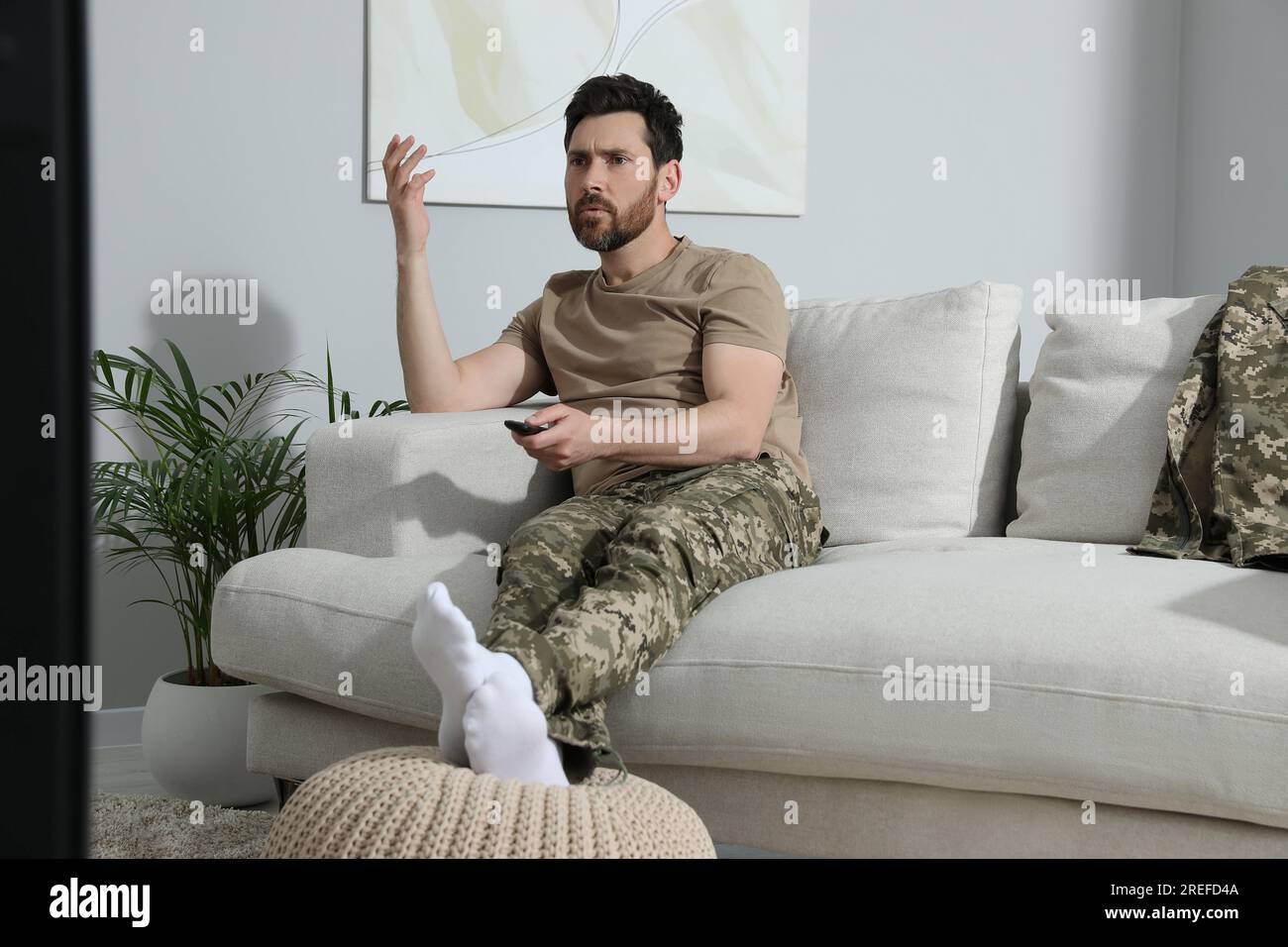 Emotional soldier watching TV on sofa in living room. Military service ...