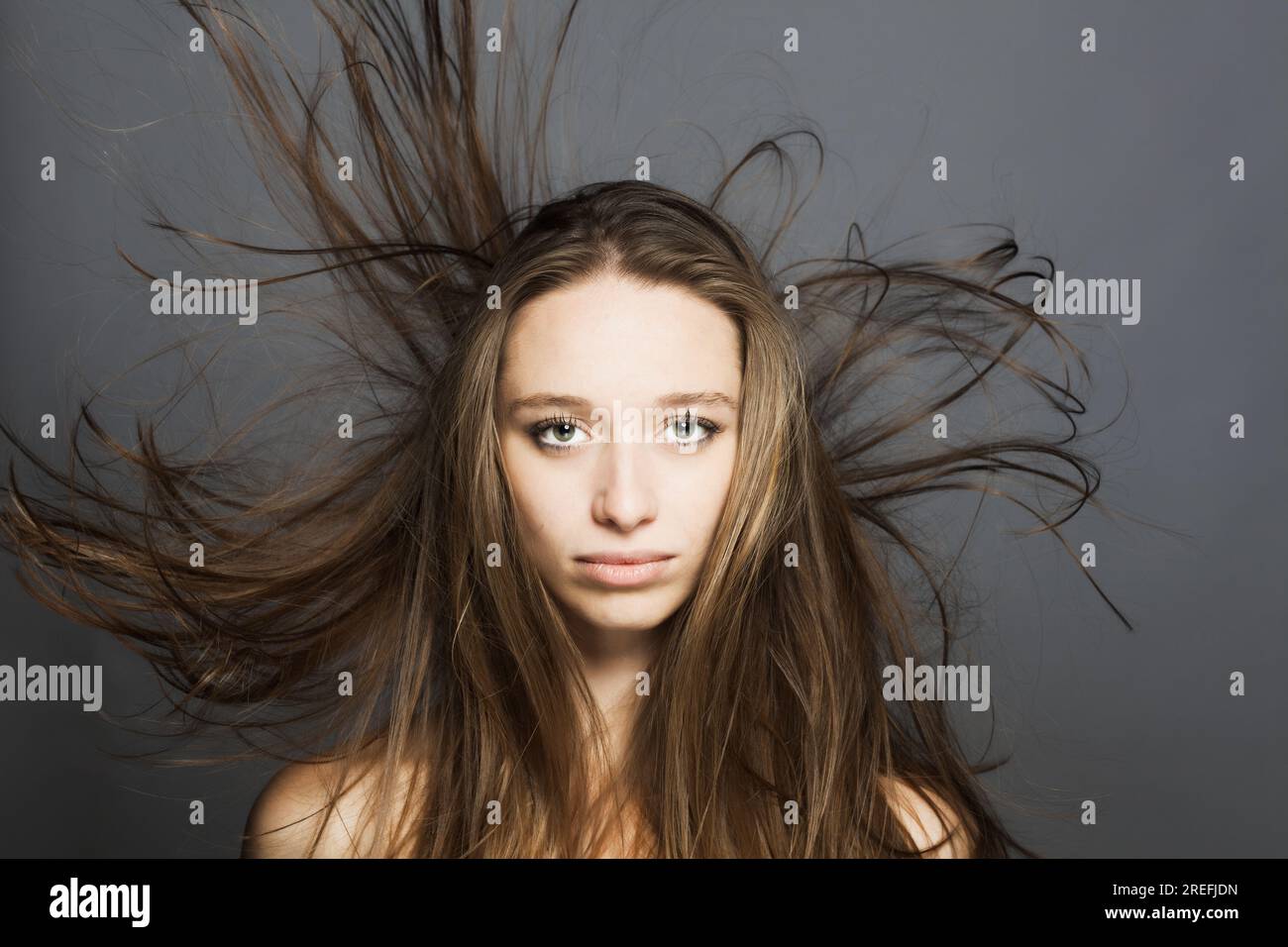 brunette girl with flowing hair in the air studio portrait against gray ...
