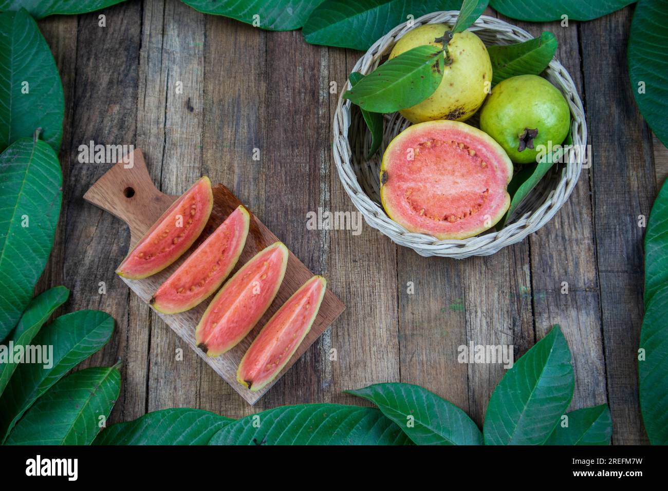 Fresh red guava in a woven bamboo basket with green leaves on a wooden ...