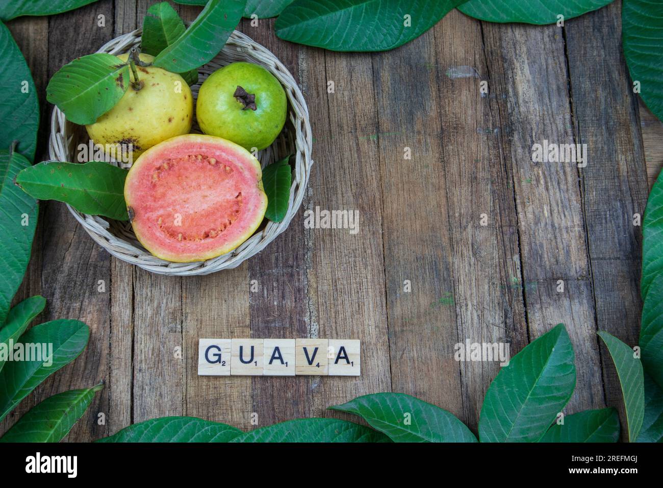 Fresh red guava in a woven bamboo basket with green leaves on a wooden ...