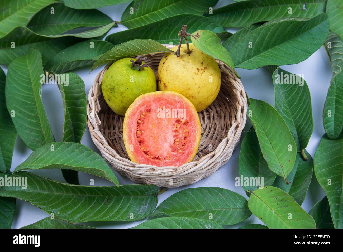 Fresh red guava in a woven bamboo basket with green leaves on a white ...