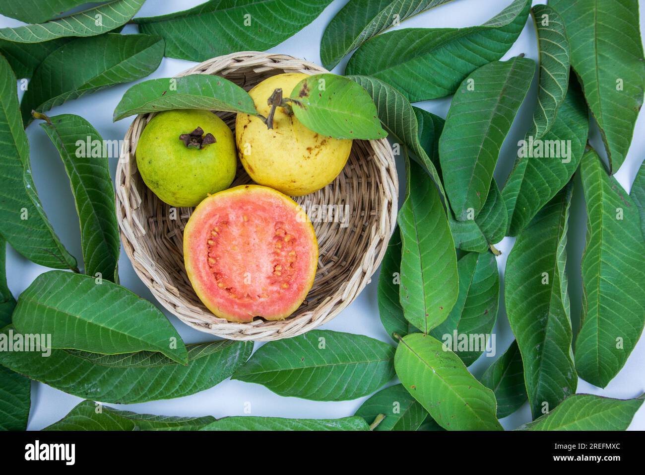 Fresh red guava in a woven bamboo basket with green leaves on a white ...