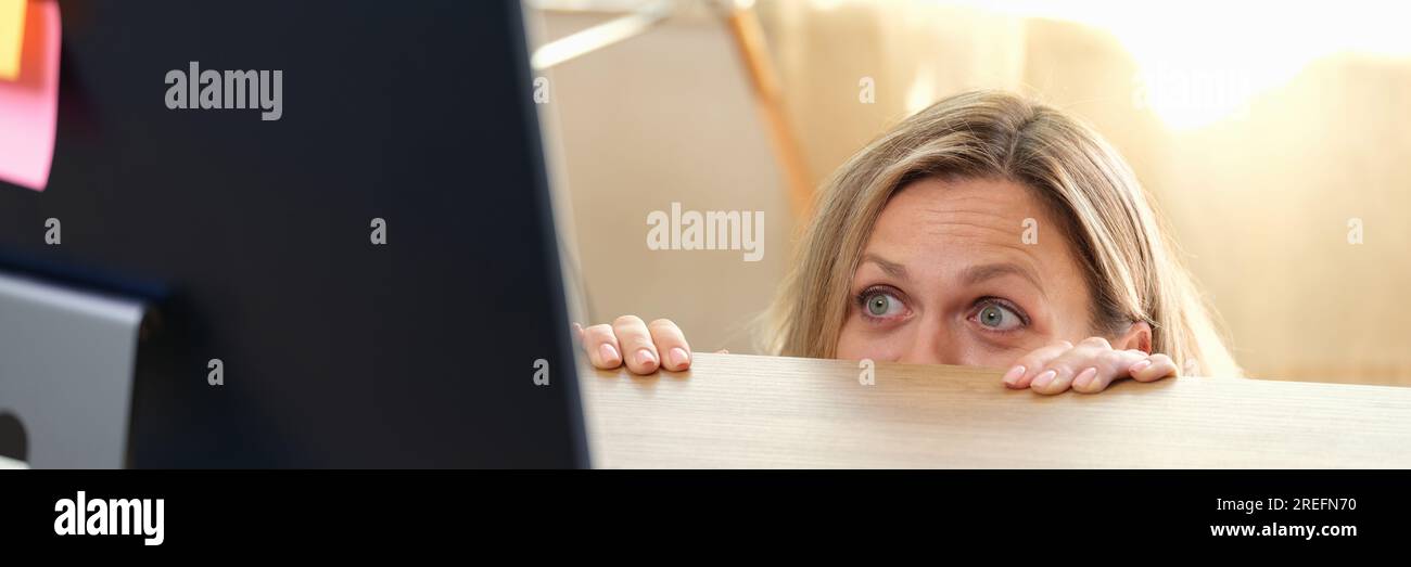 Woman hides behind office desk and looks at computer monitor Stock ...