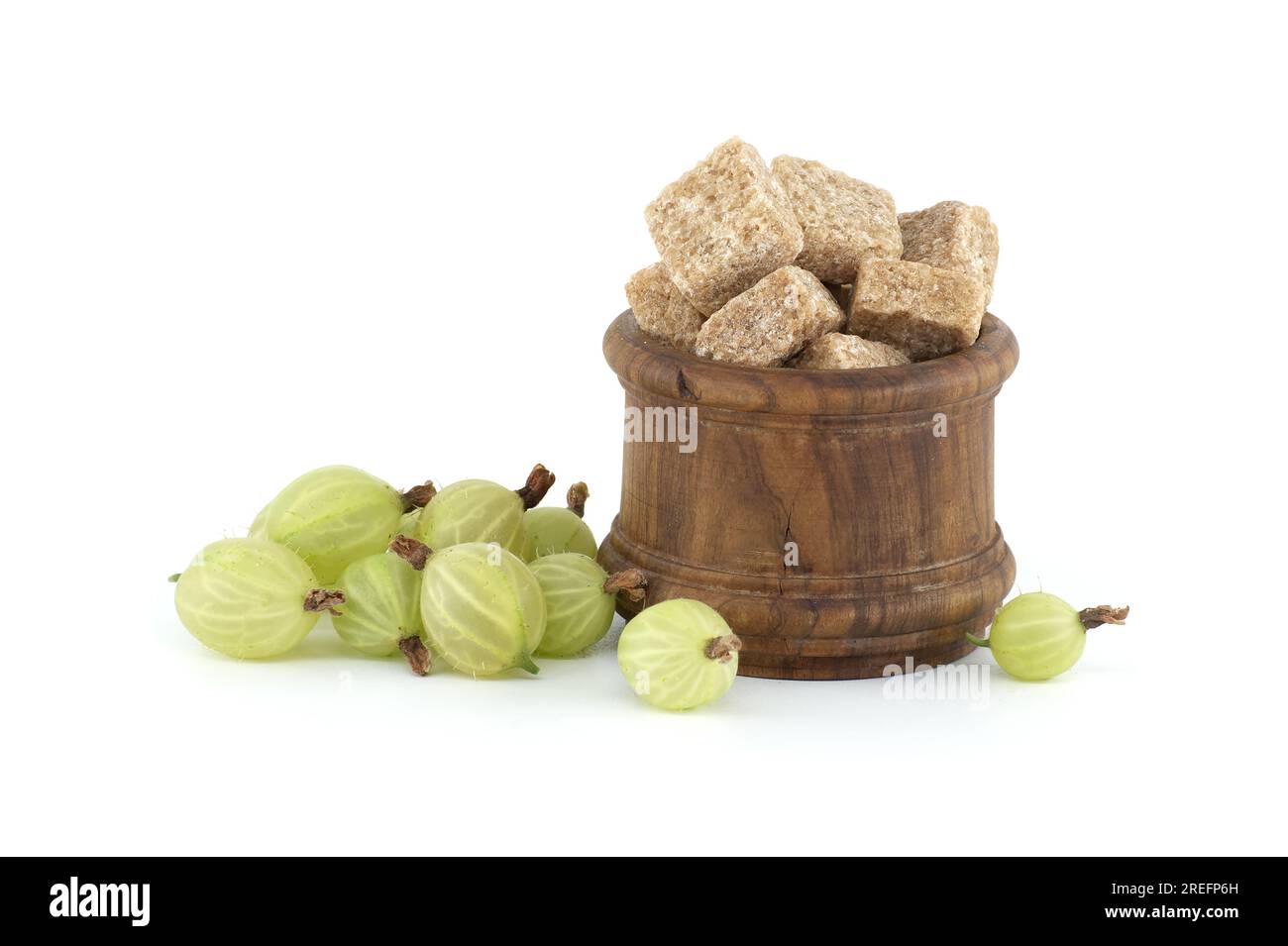 Green ripe gooseberries next to brown cane sugar cubes in wooden bowl ...