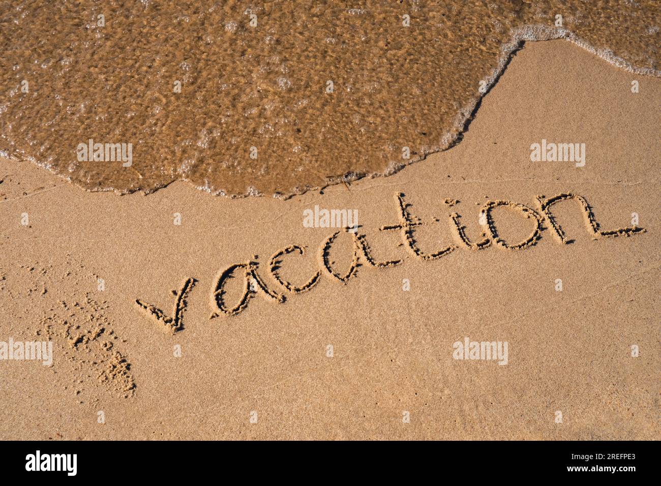 Text VACATION handwritten in sand surface. Blue ocean wave washing away ...