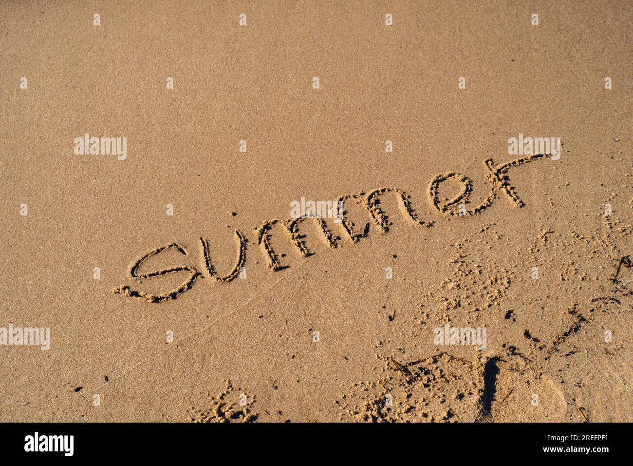 Text SUMMER handwritten in sand surface. Blue ocean wave washing away ...