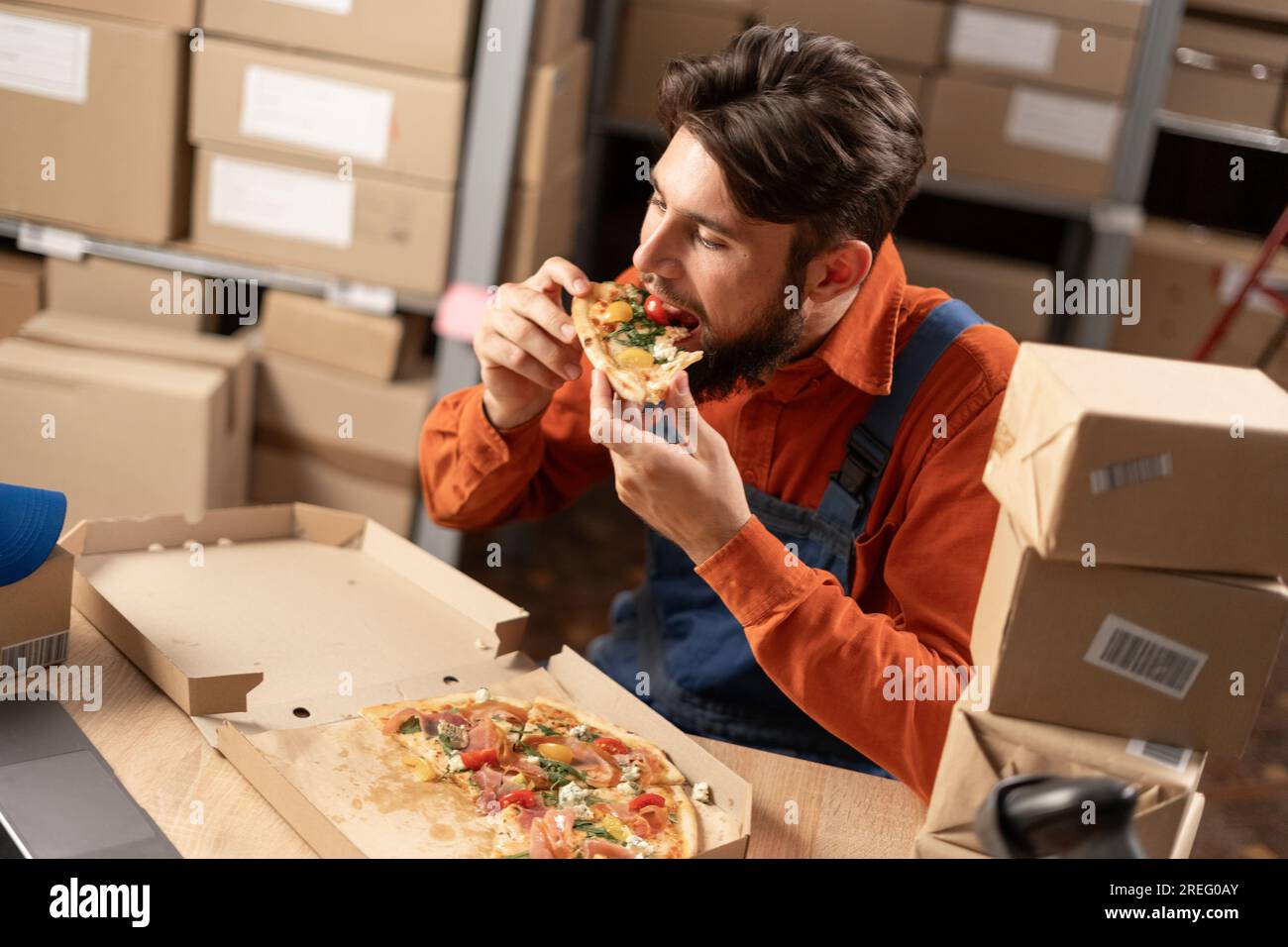 Male warehouse worker eating delicious pizza at lunch or dinner while ...