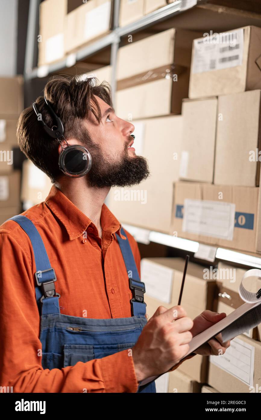 male worker wearing headset in logistics distribution warehouse writing ...