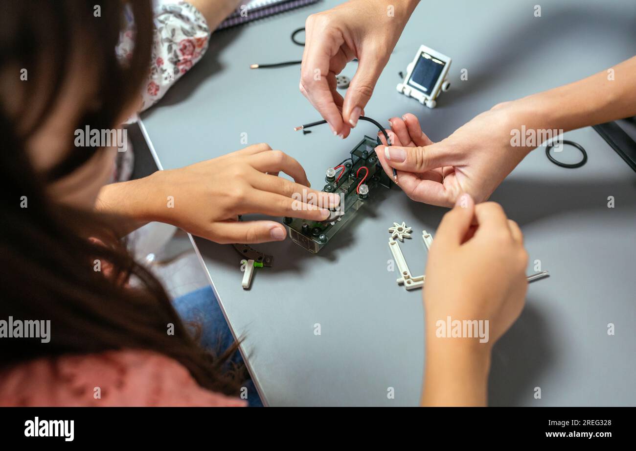 Female teacher helping girl student to assemble electrical circuit in a ...