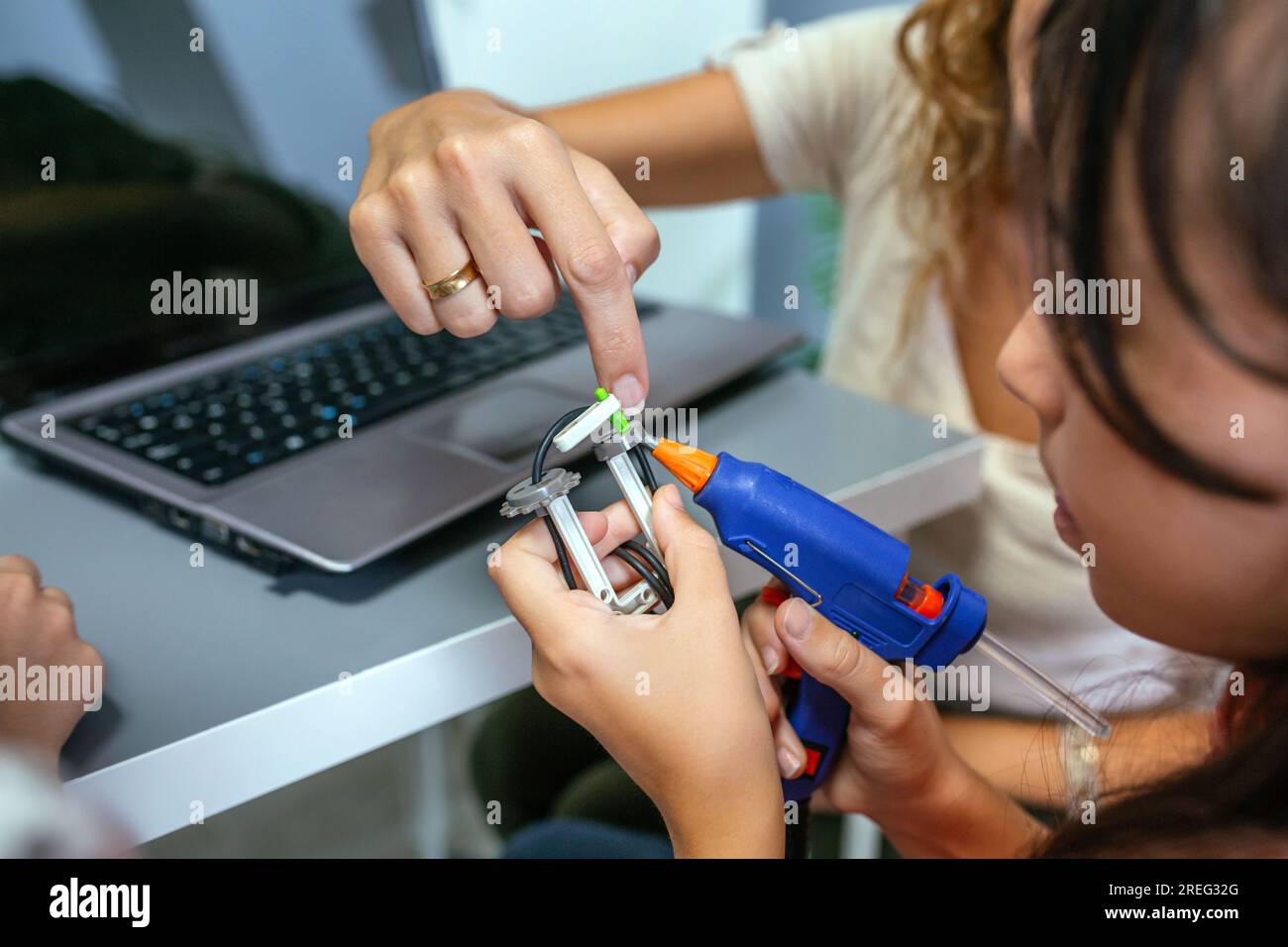 Teacher helping to student using hot melt glue gun on machine pieces in ...