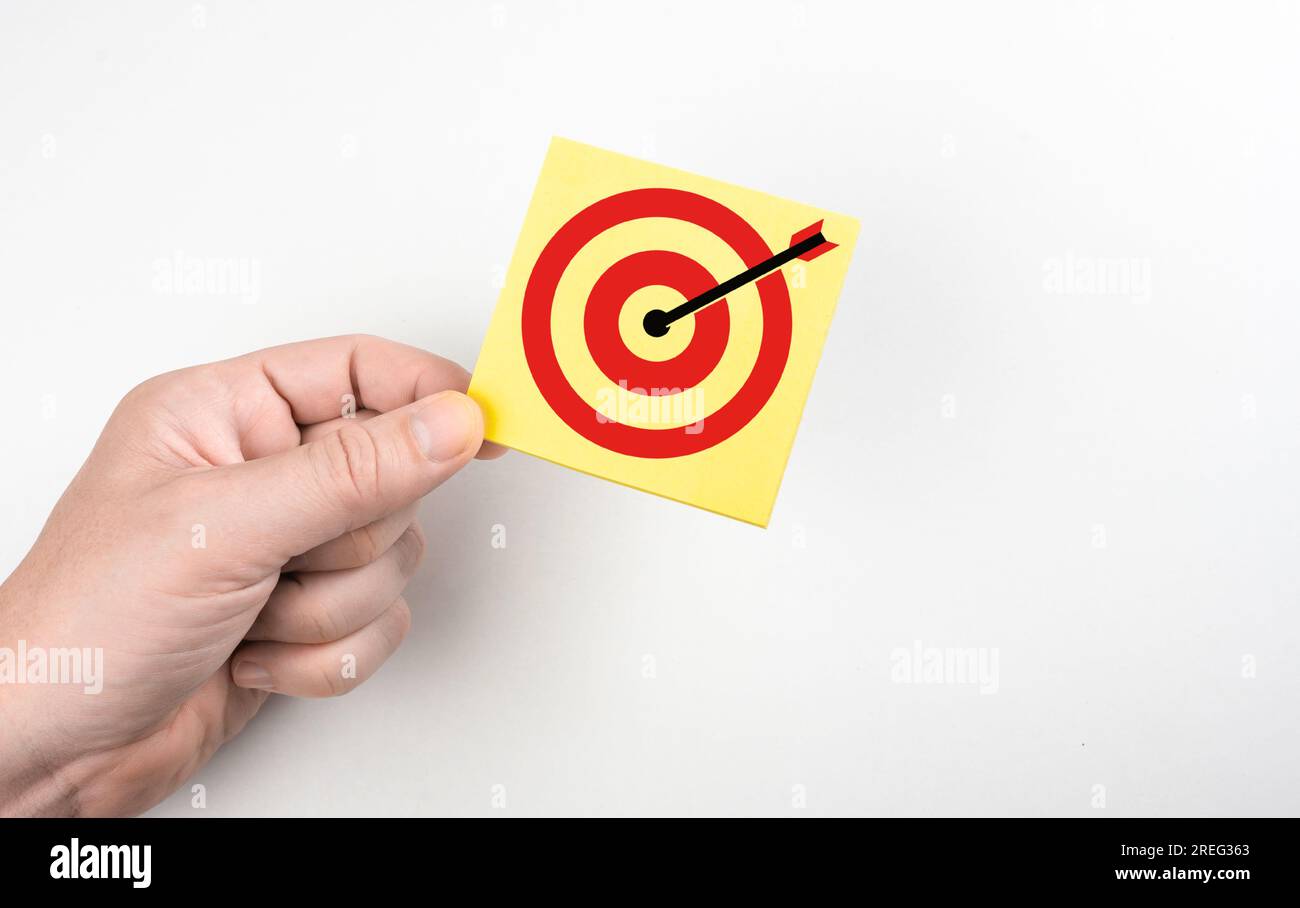 Hand holding yellow paper sticky note with target, goal, aim. Setting ...