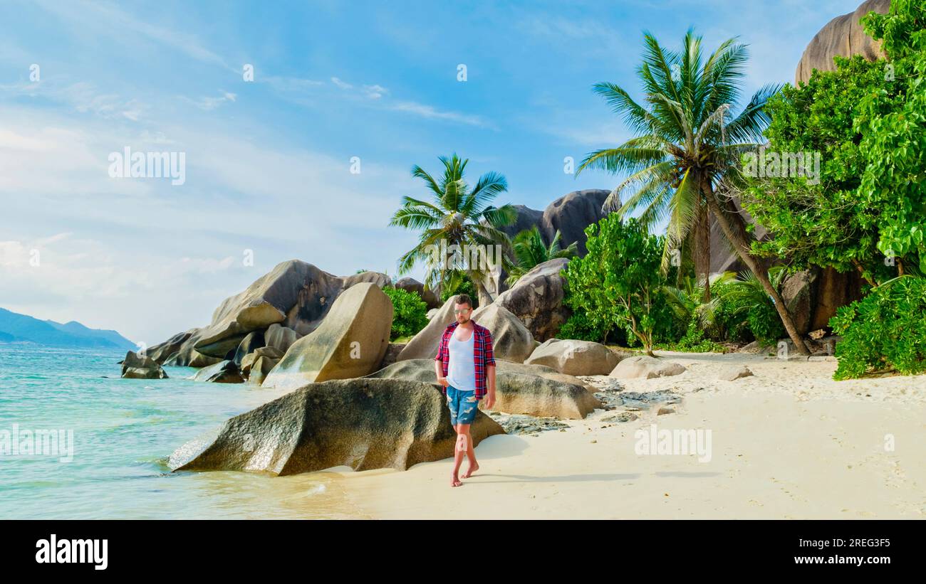 Young men walking at a white tropical beach Anse Source d'Argent beach ...