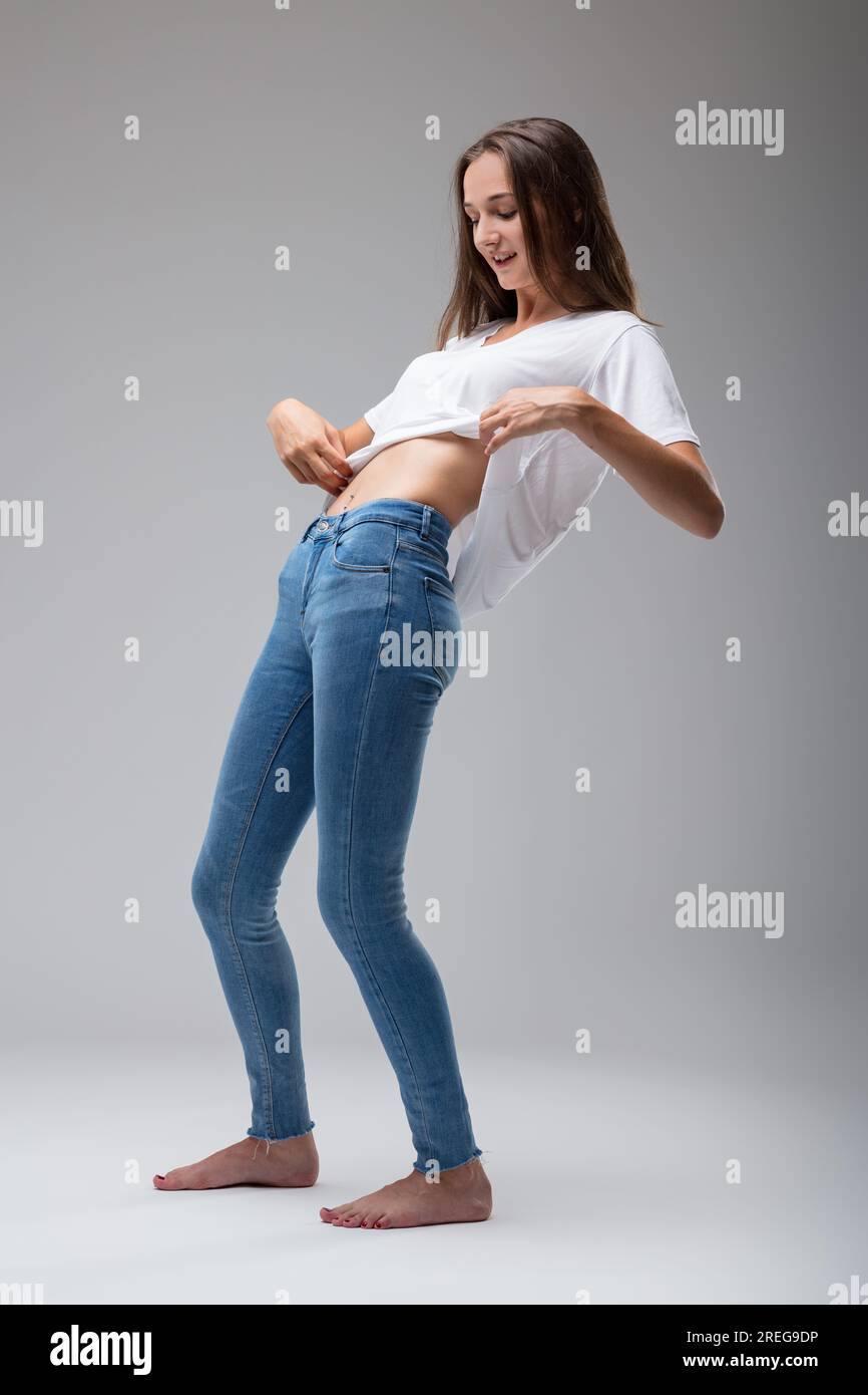 full-length portrait captures a young woman in jeans, lifting her white ...