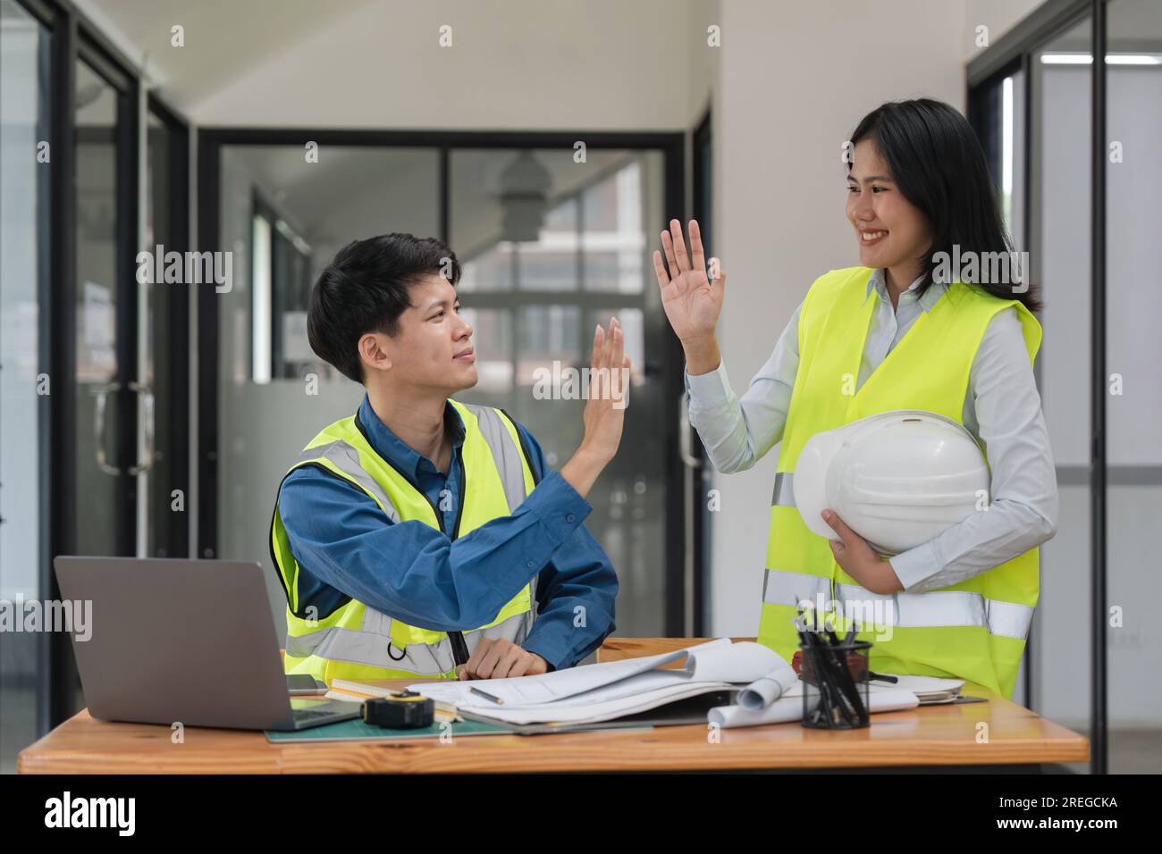 Construction engineer with blueprint making high five while standing on ...
