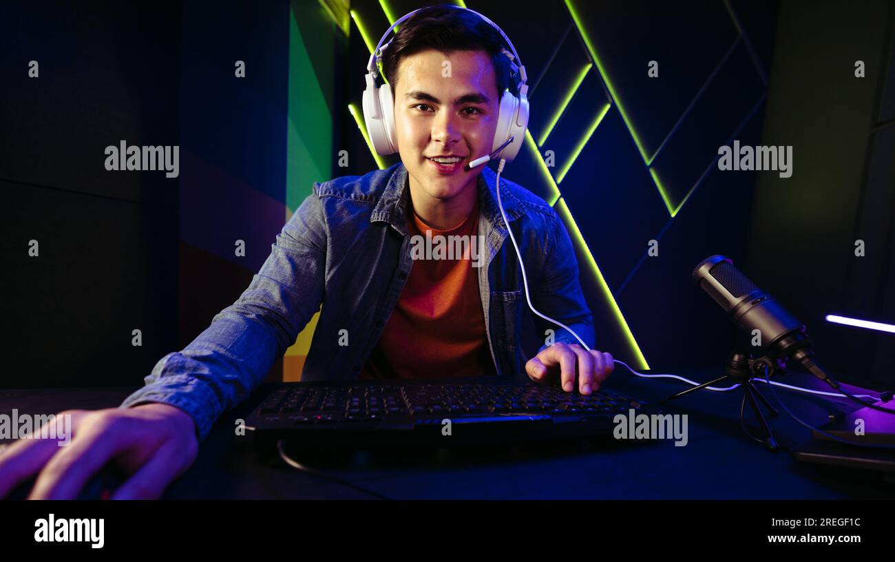 Happy young man sitting at a gaming computer with a headset, playing a ...