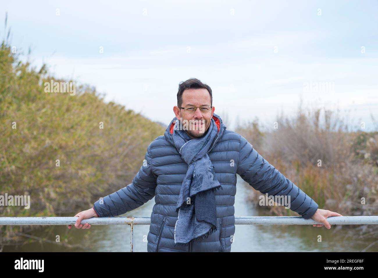 Full length portrait of smiling adult man standing by railing on bridge ...