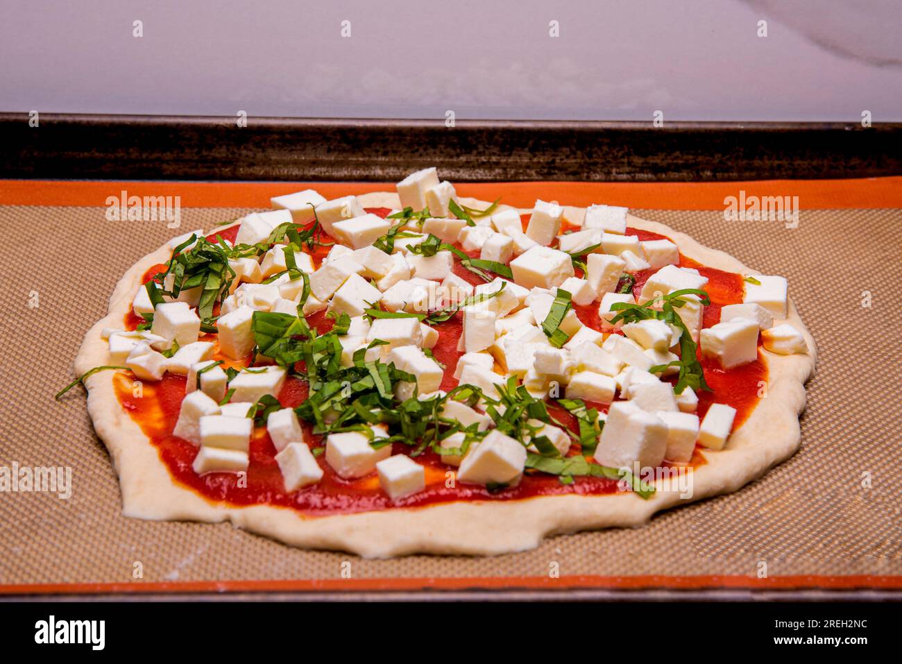 Uncooked cheese and basil pizza on sheet pan preparing to be cooked ...
