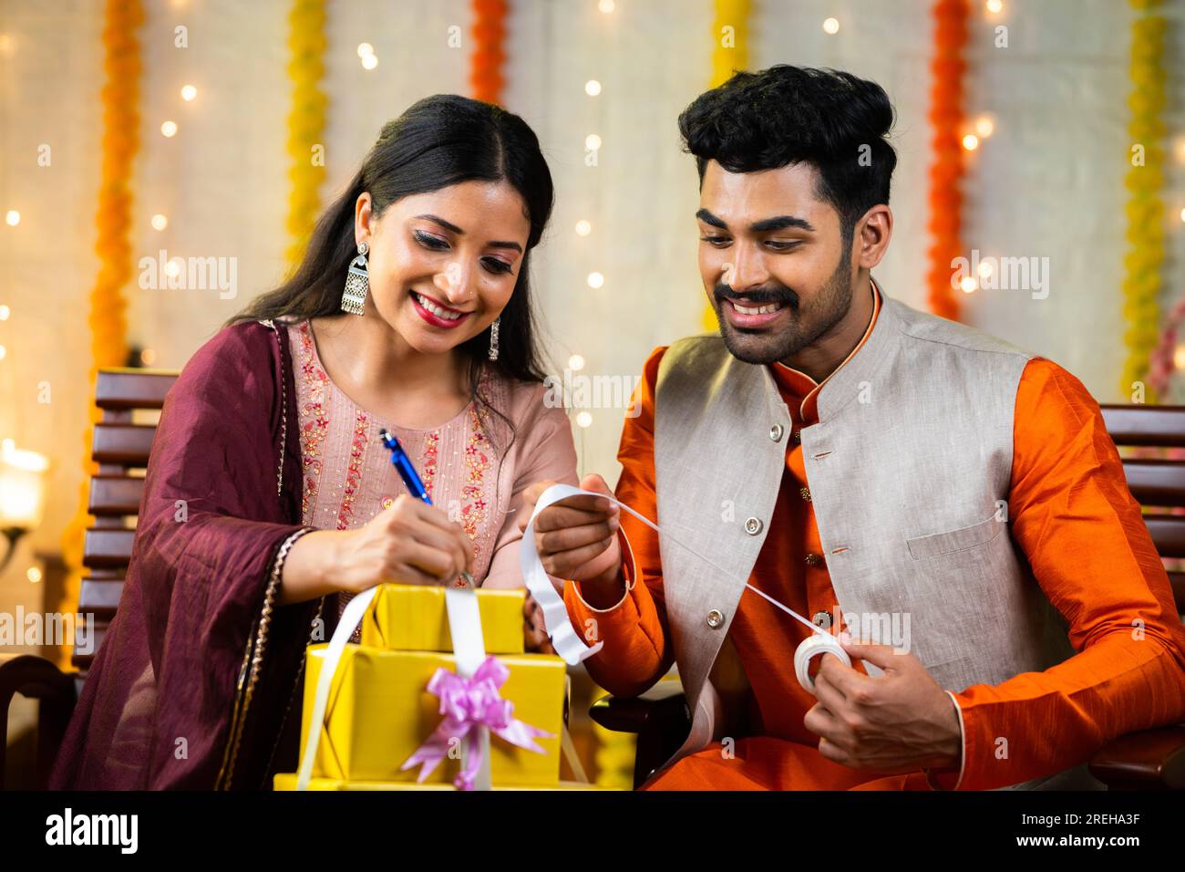 Happy indian married couple busy preparing gift box by writing names ...