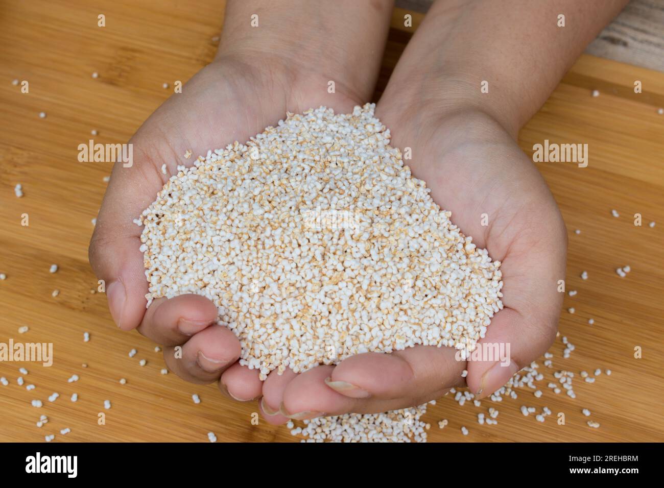 Hand holding puffed amaranth or ramdana or rajgira on a wooden tray. It ...