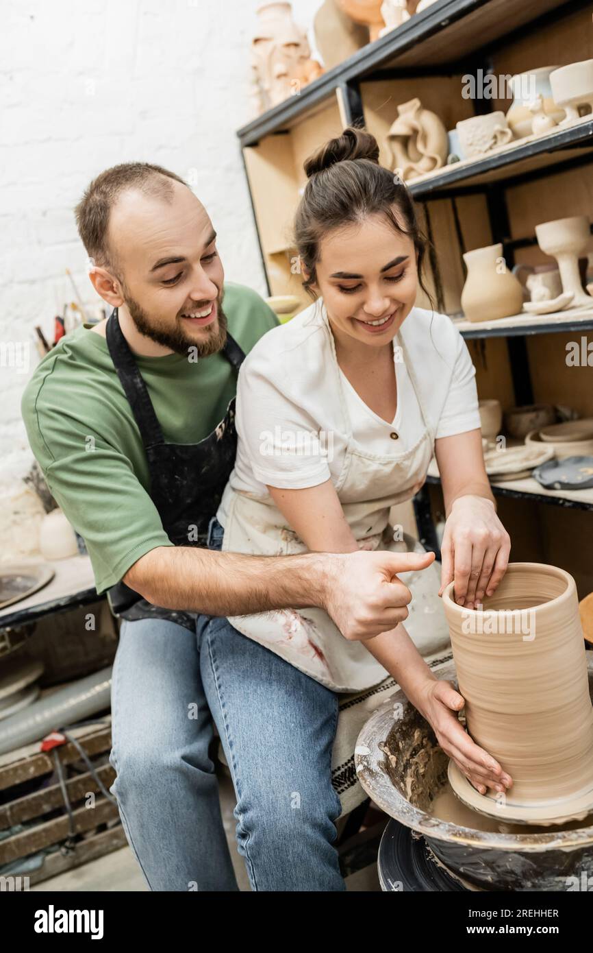 Positive sculptor talking to girlfriend making clay vase on pottery ...