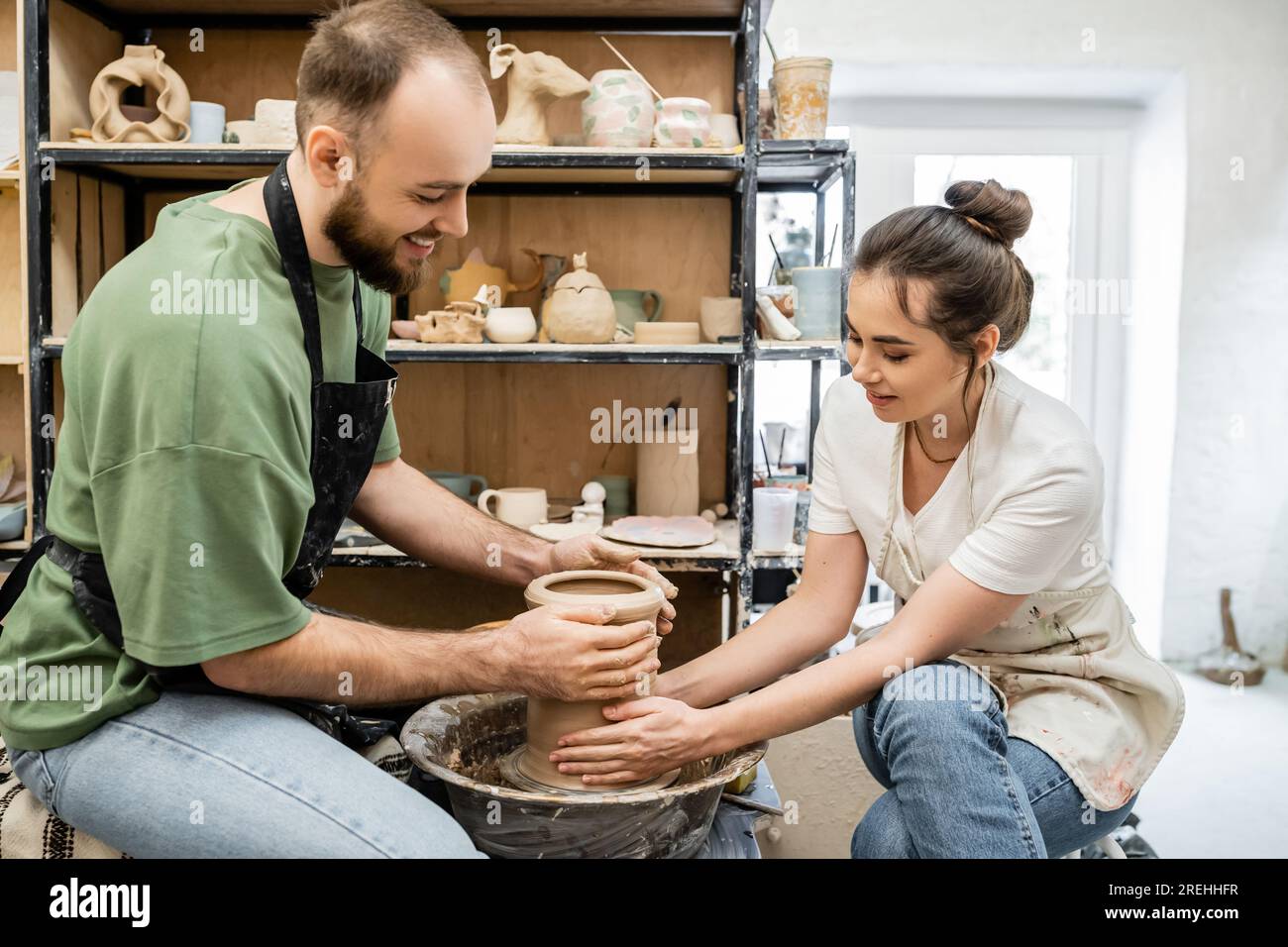 Positive couple of potters shaping clay vase on pottery wheel together ...