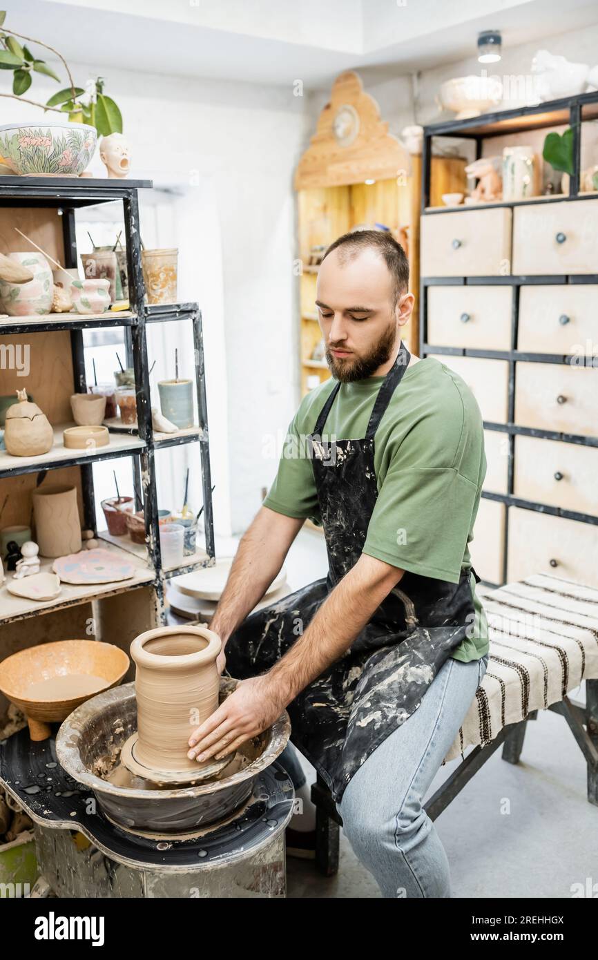 Bearded craftsman in dirty apron shaping and forming clay on pottery ...
