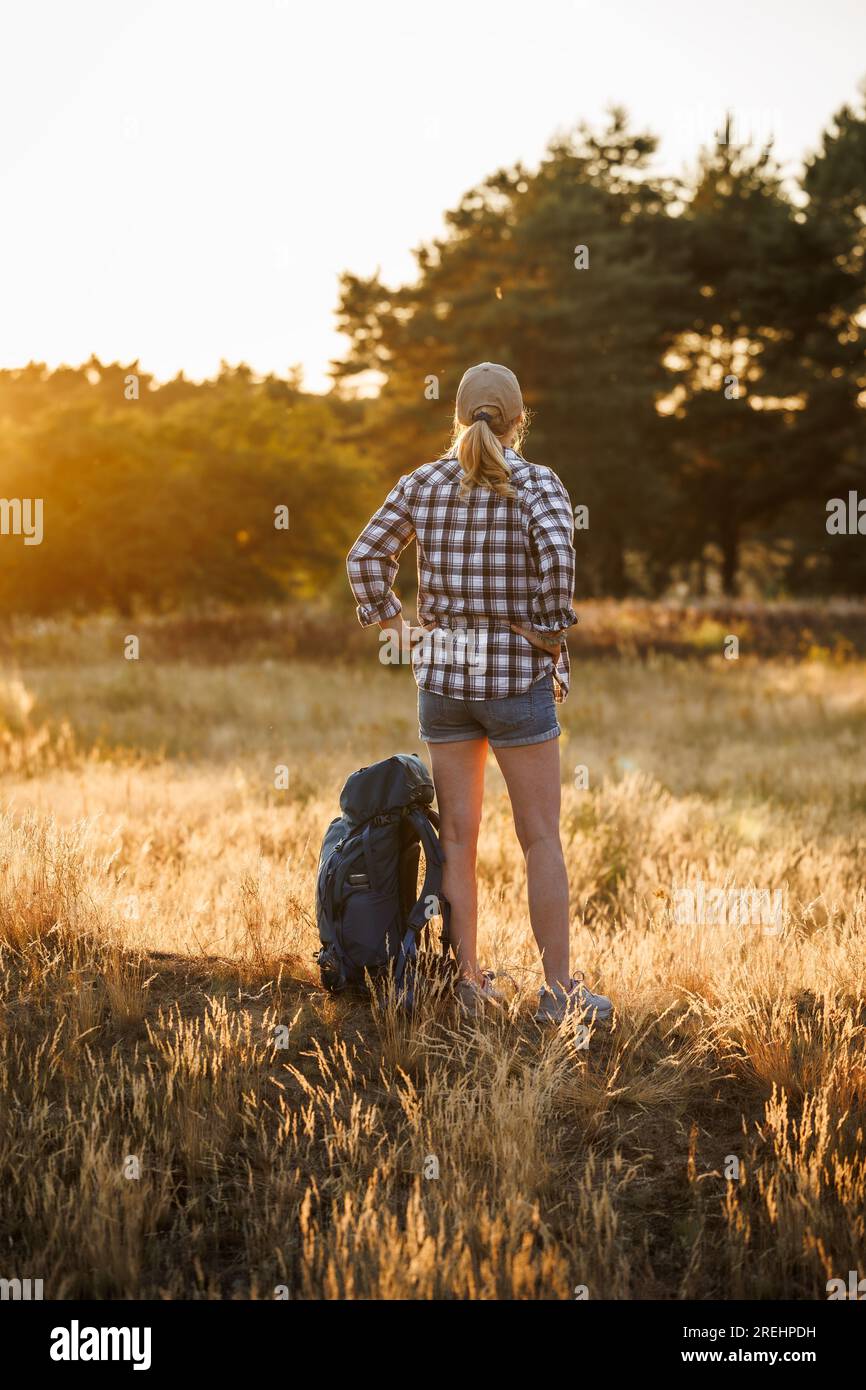 Woman with backpack is resting in nature and enjoying summer sunset ...