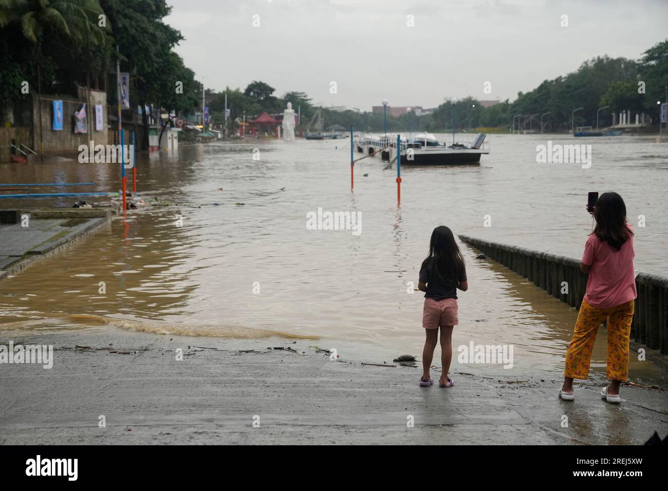 Girls look at a flooded riverside park due to enhanced rains brought ...