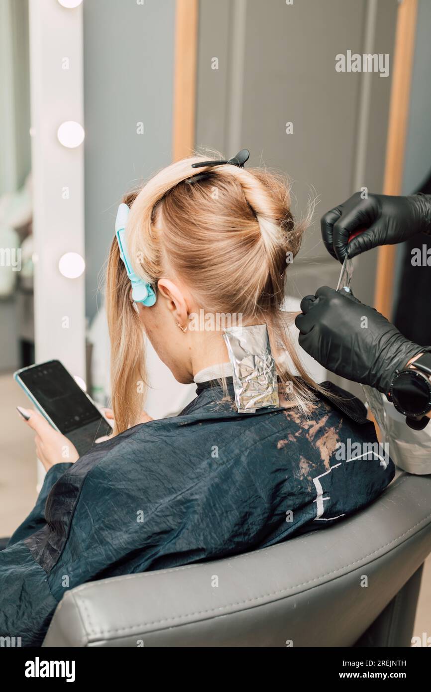 The process of hair coloring in a beauty salon. Blonde dyeing her hair ...