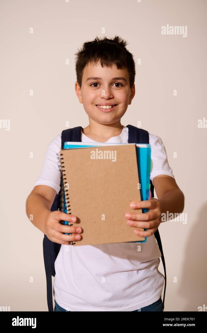 Smiling happy school child holding out at camera copybook with copy ...