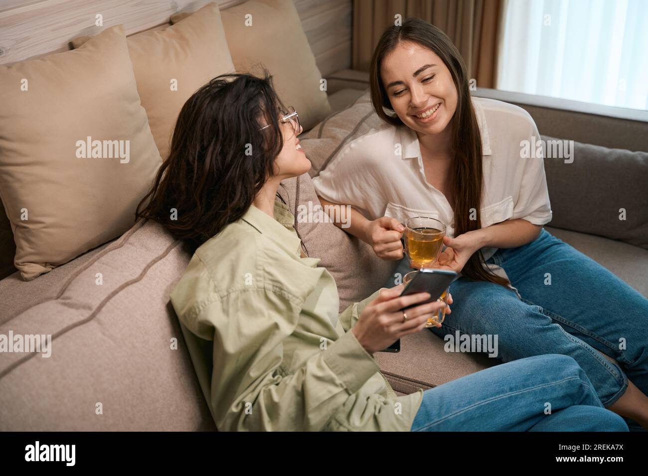 Two young ladies having conversation while sitting on couch Stock Photo ...