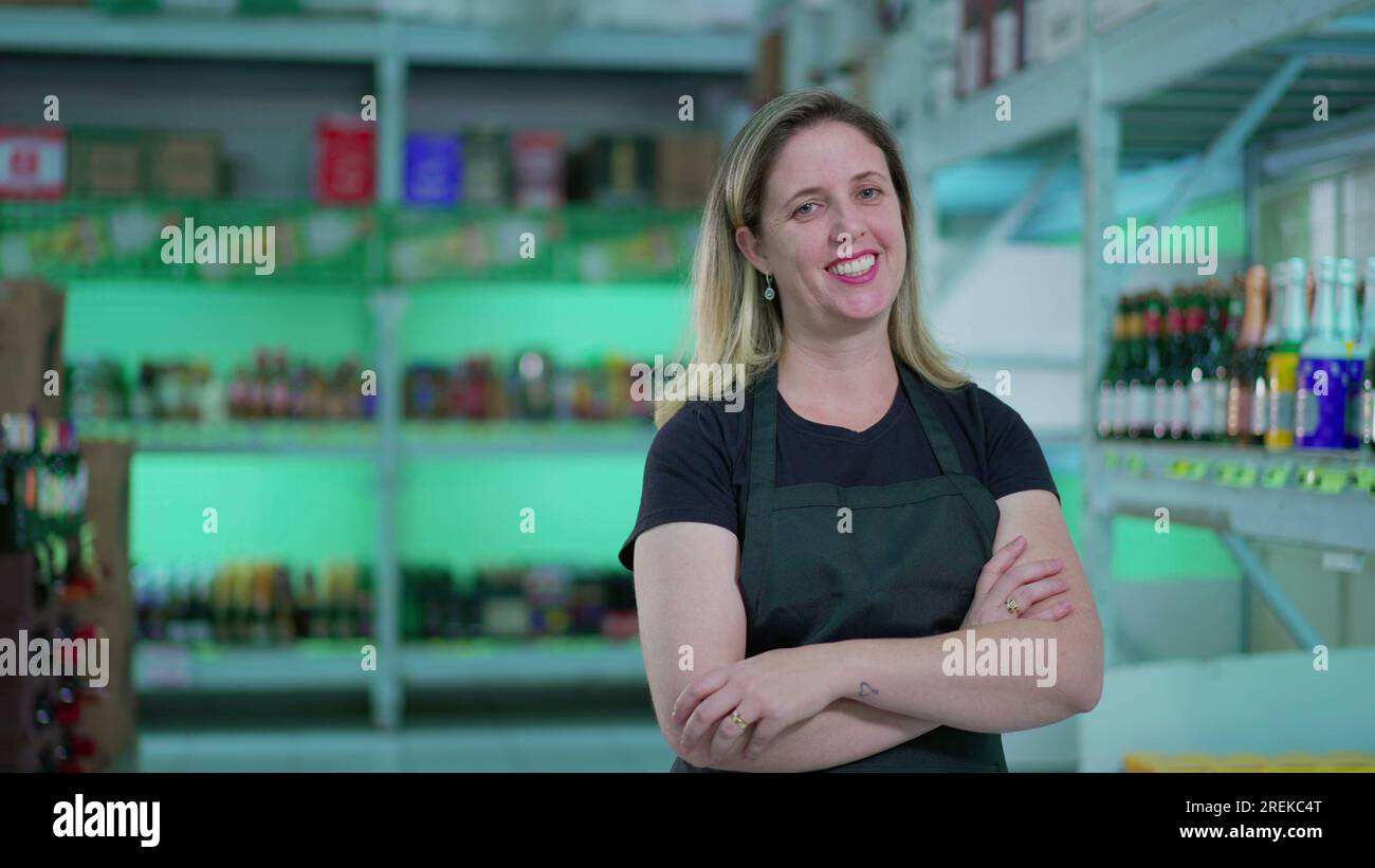 Happy female employee of Supermarket standing at aisle with arms ...