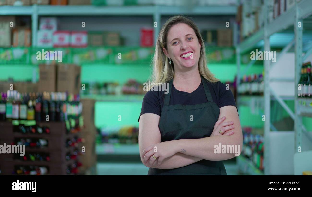 Happy female employee of Supermarket standing at aisle with arms ...