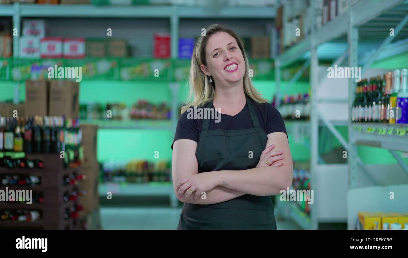 Happy female employee of Supermarket standing at aisle with arms ...