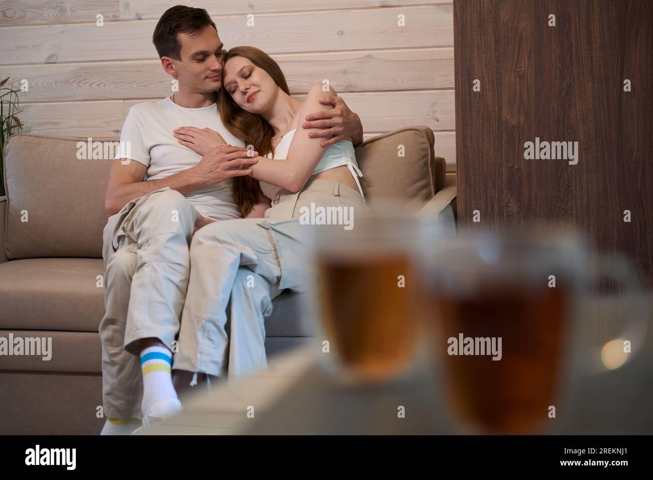 Happy couple hugging while sitting on sofa at home Stock Photo - Alamy