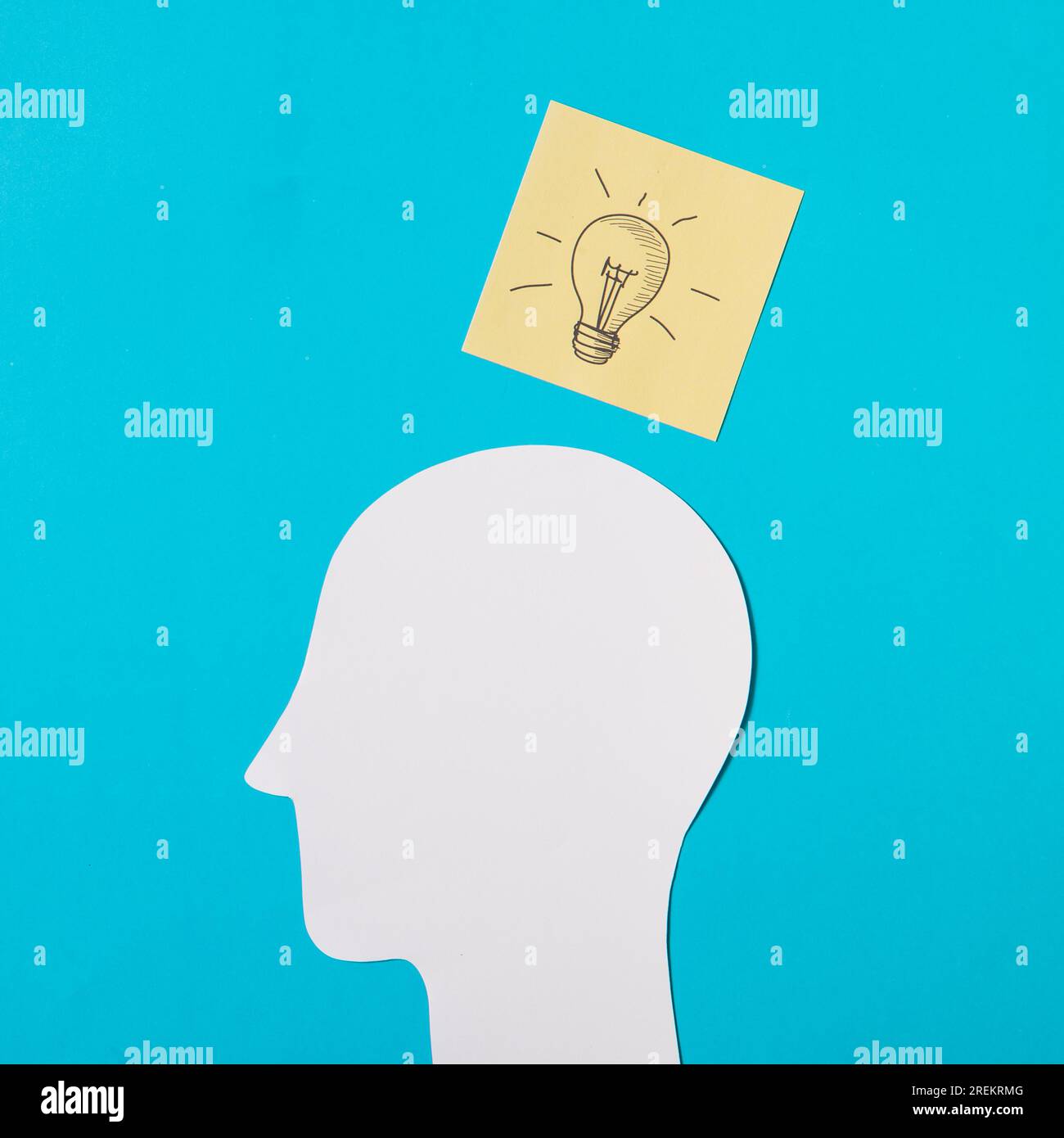 Drawn light bulb icon sticky note paper cut out head against blue ...