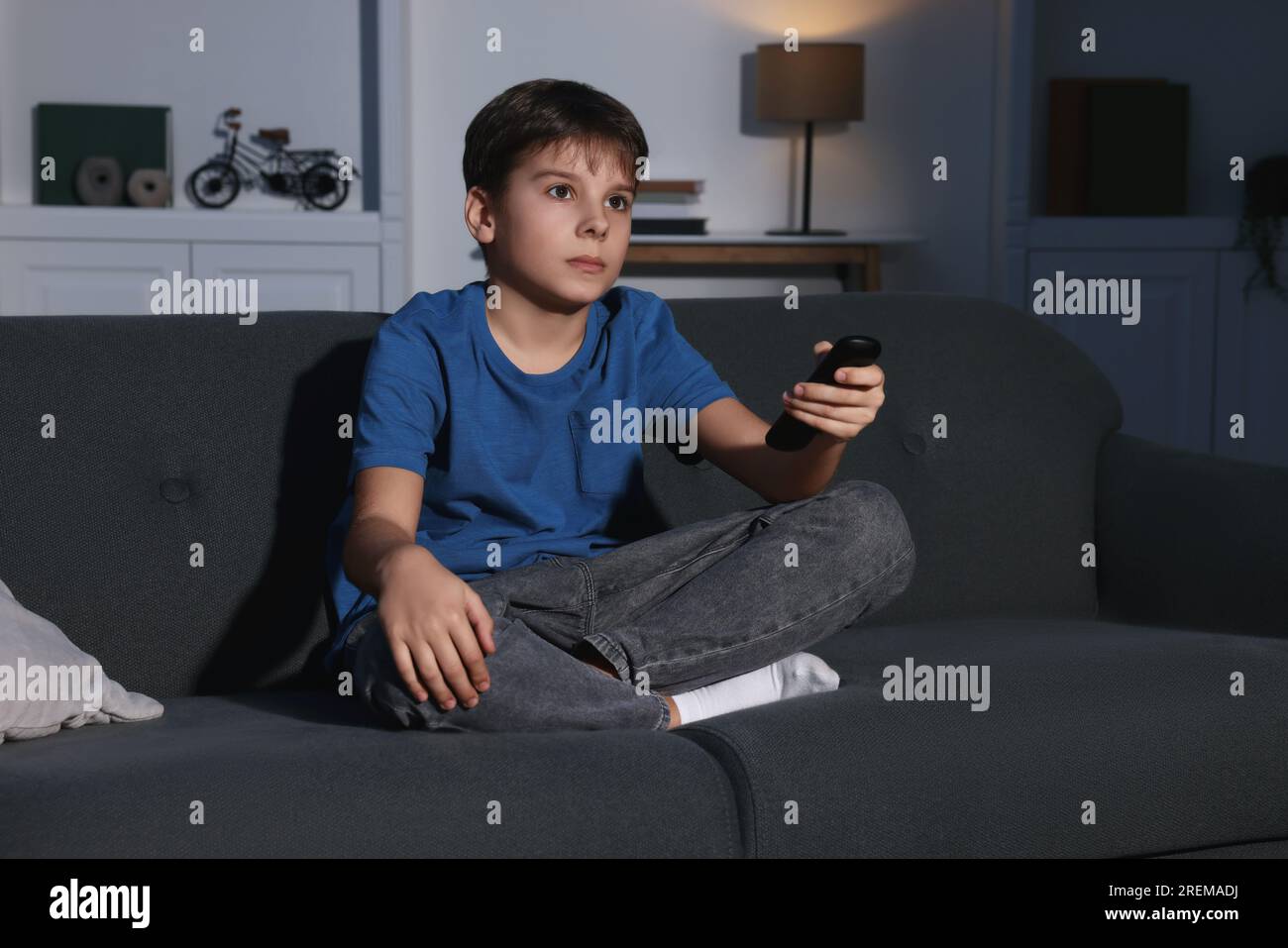 Little boy changing TV channels with remote control on sofa at home ...