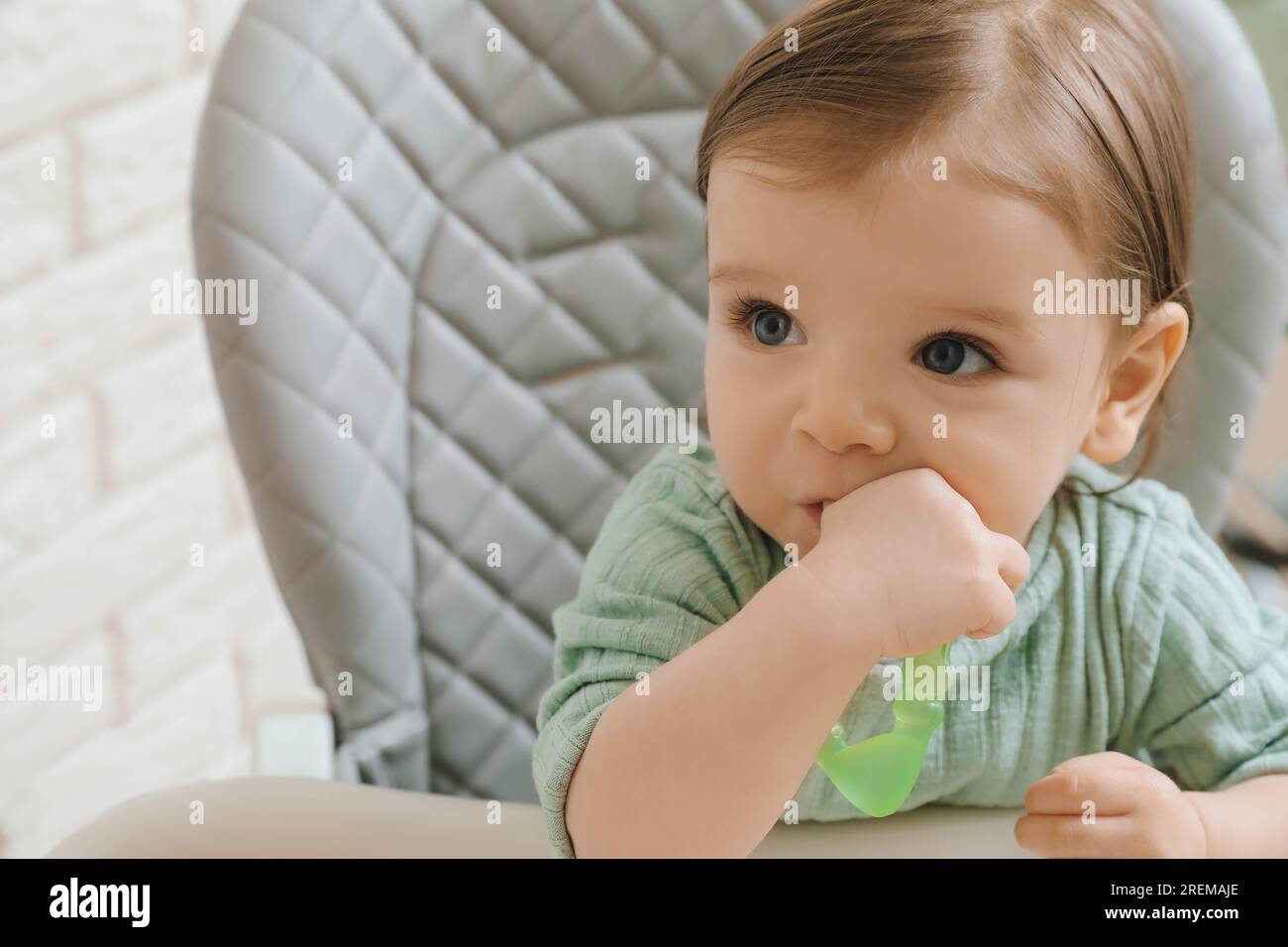 Cute little baby nibbling teether in high chair indoors, closeup. Space ...