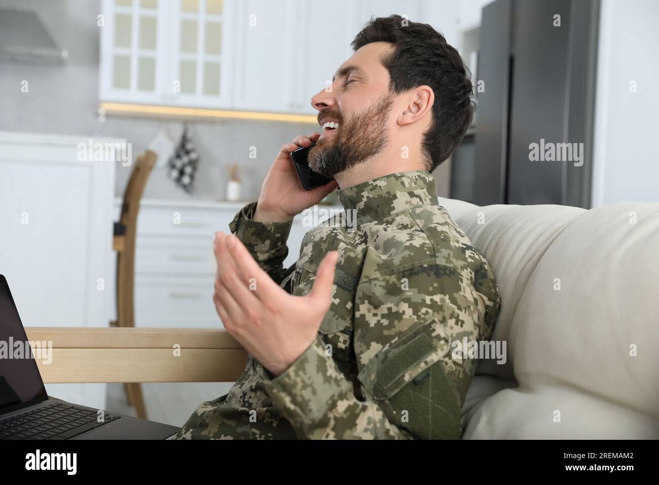 Happy soldier with laptop talking on phone at home. Military service ...