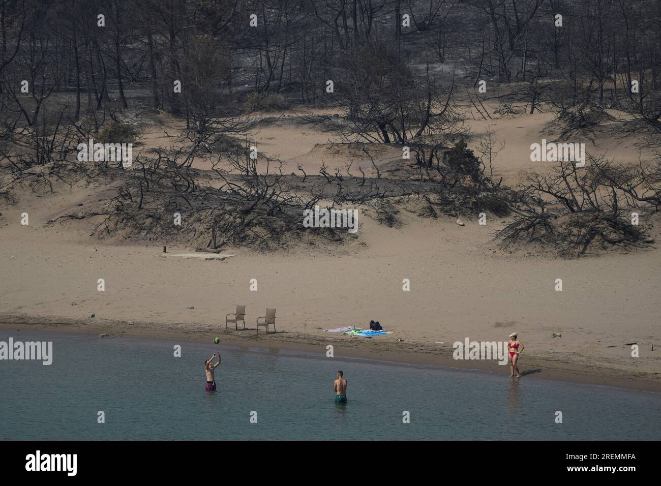 People play with a ball in front of a burnt forest at a beach of ...