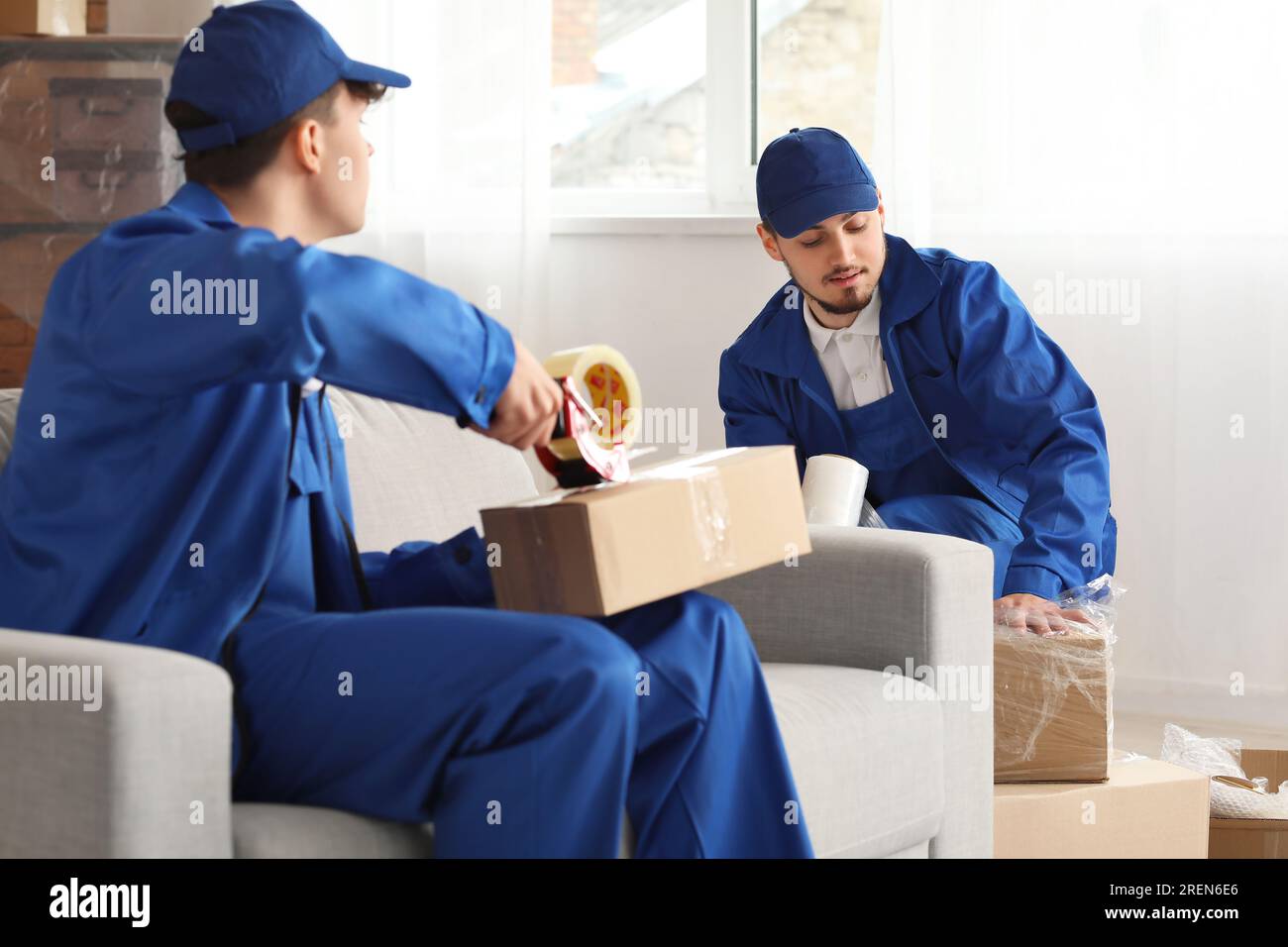 Male movers wrapping boxes in room Stock Photo - Alamy