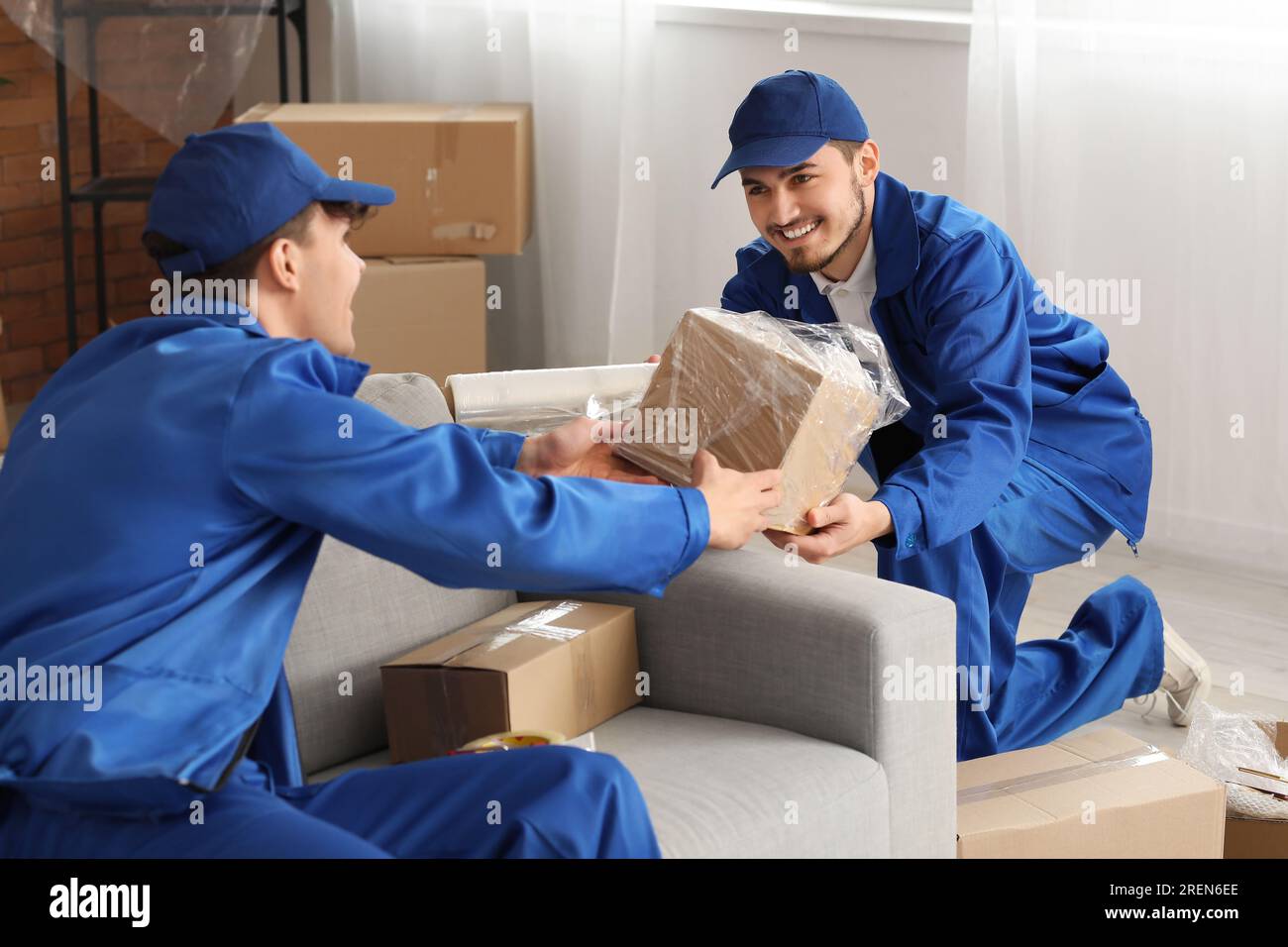 Male movers wrapping box with stretch film in room Stock Photo - Alamy