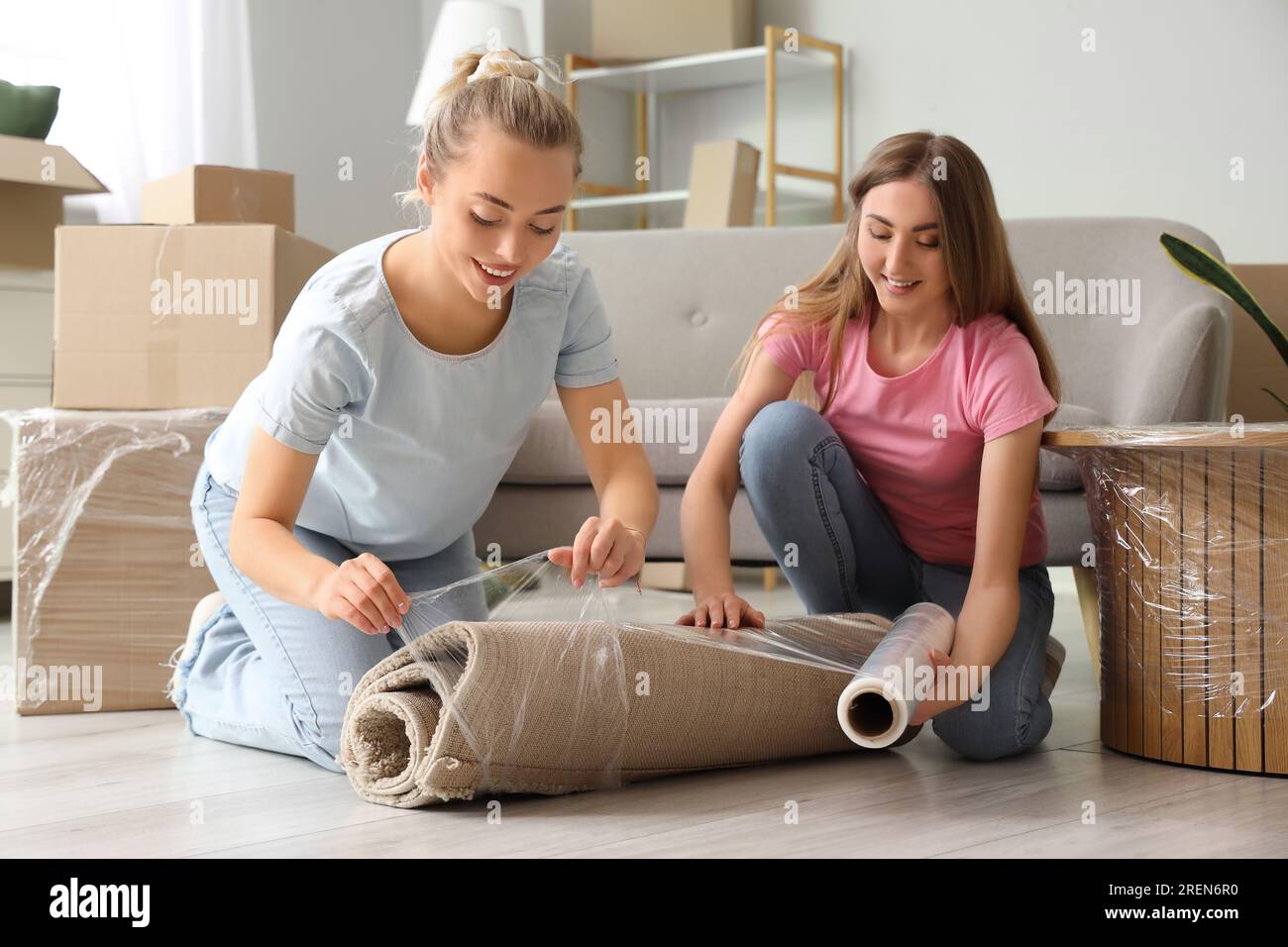 Young women wrapping carpet with stretch film at home Stock Photo - Alamy
