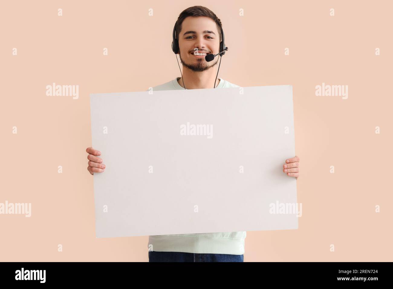 Male technical support agent with blank poster on beige background ...